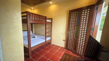 Um quarto com uma cama beliche, uma porta de madeira com padrão de grade e um chão de ladrilhos vermelhos.