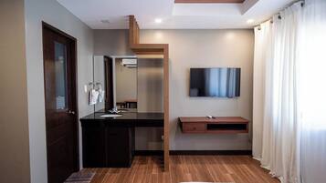 Quarto de hotel moderno com piso de madeira, escrivaninha preta com espelho, TV de tela plana na parede e cama com roupa de cama branca.