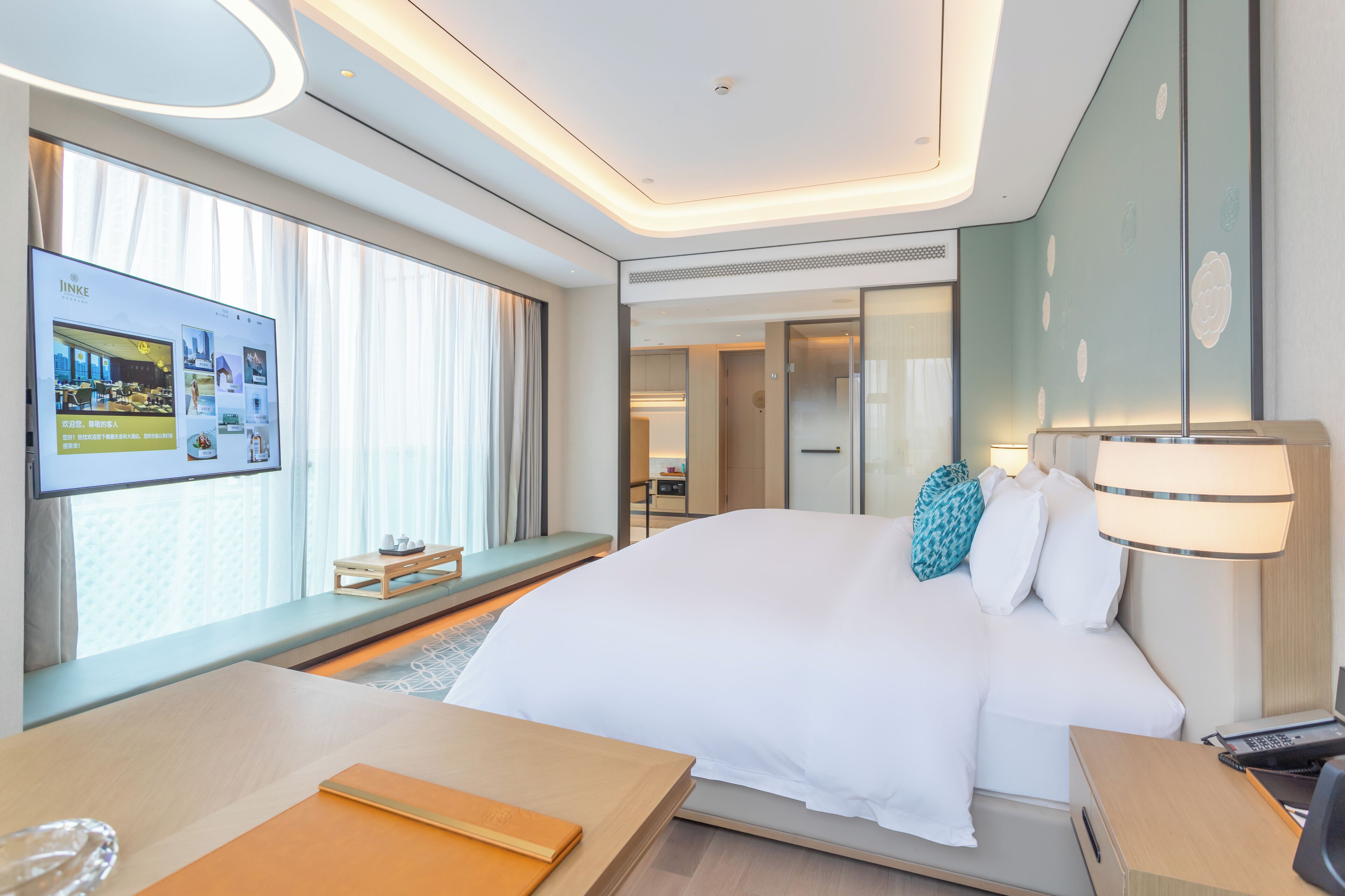 Quarto de hotel moderno com uma cama grande, uma mesa de cabeceira, televisão na parede e uma janela com cortinas.