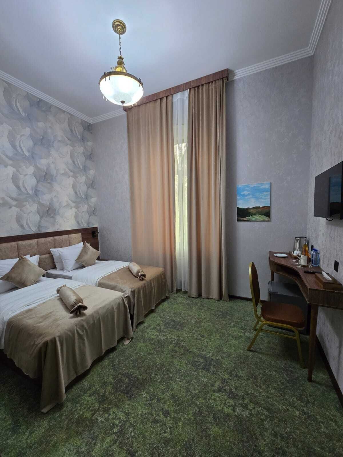 Quarto de hotel com duas camas, uma mesa, uma cadeira, uma televisão e uma janela grande com cortinas.