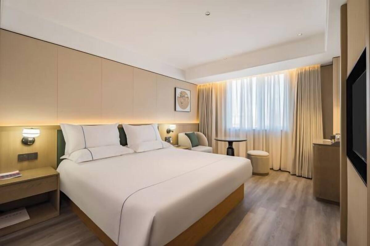 Quarto de hotel moderno com uma cama grande, mesas de cabeceira, uma pequena mesa redonda e uma televisão.
