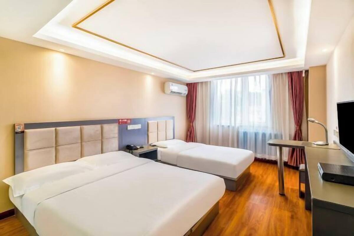 Quarto de hotel com duas camas, uma escrivaninha, uma TV e uma janela com cortinas.