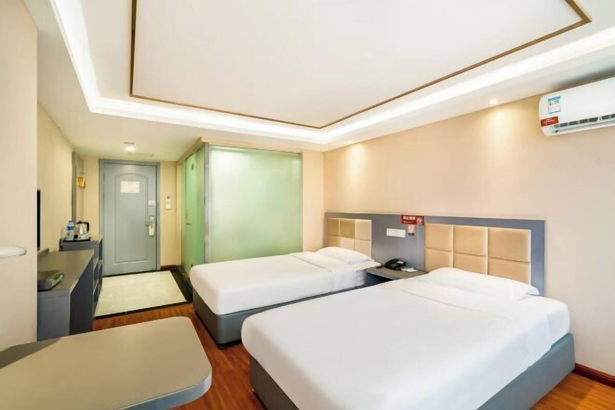 Quarto de hotel com duas camas de solteiro, uma escrivaninha, uma cadeira e uma kitchenette pequena.