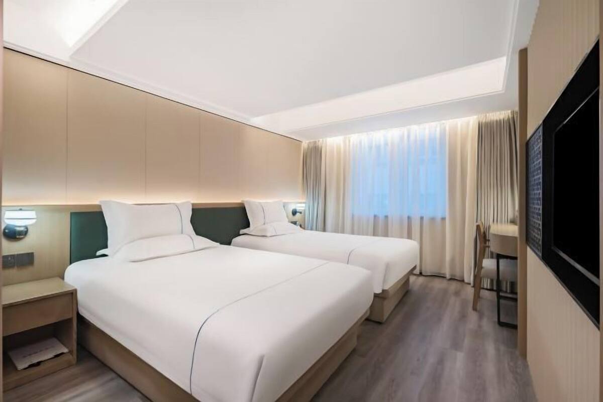 Quarto de hotel com duas camas, uma mesa, uma cadeira e uma televisão.