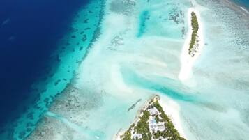 Vista aérea de uma ilha tropical com águas azul-turquesa cristalinas, uma pequena área de praia e um conjunto de edifícios, provavelmente parte de um resort.