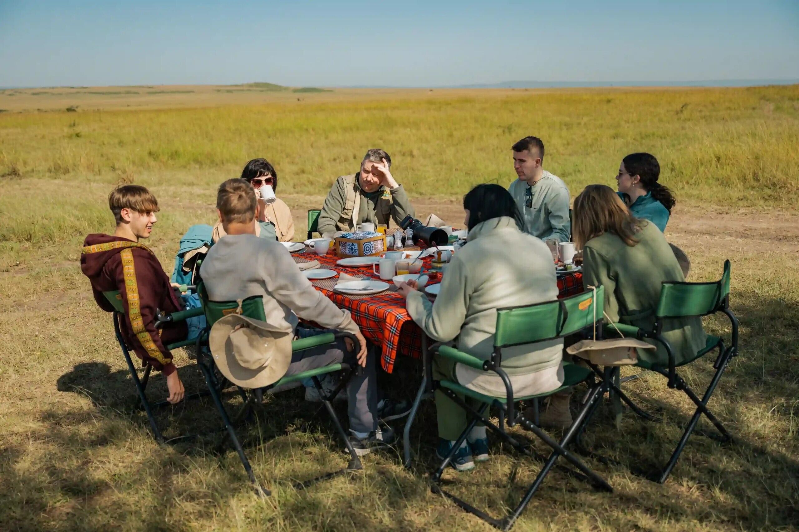 Um grupo de pessoas sentadas à volta de uma mesa em um campo aberto com céu claro.