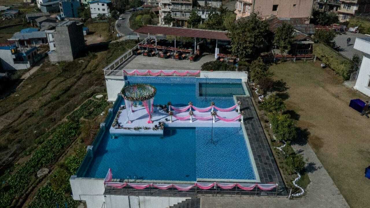 Vista aérea de um hotel com piscina, área coberta com assentos e jardim.