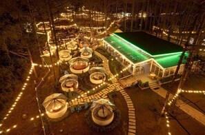Um hotel com telhado verde, várias estruturas circulares com guarda-sóis e um caminho iluminado.