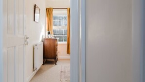 Um corredor com radiador, cómoda de madeira e janela com cortinas.