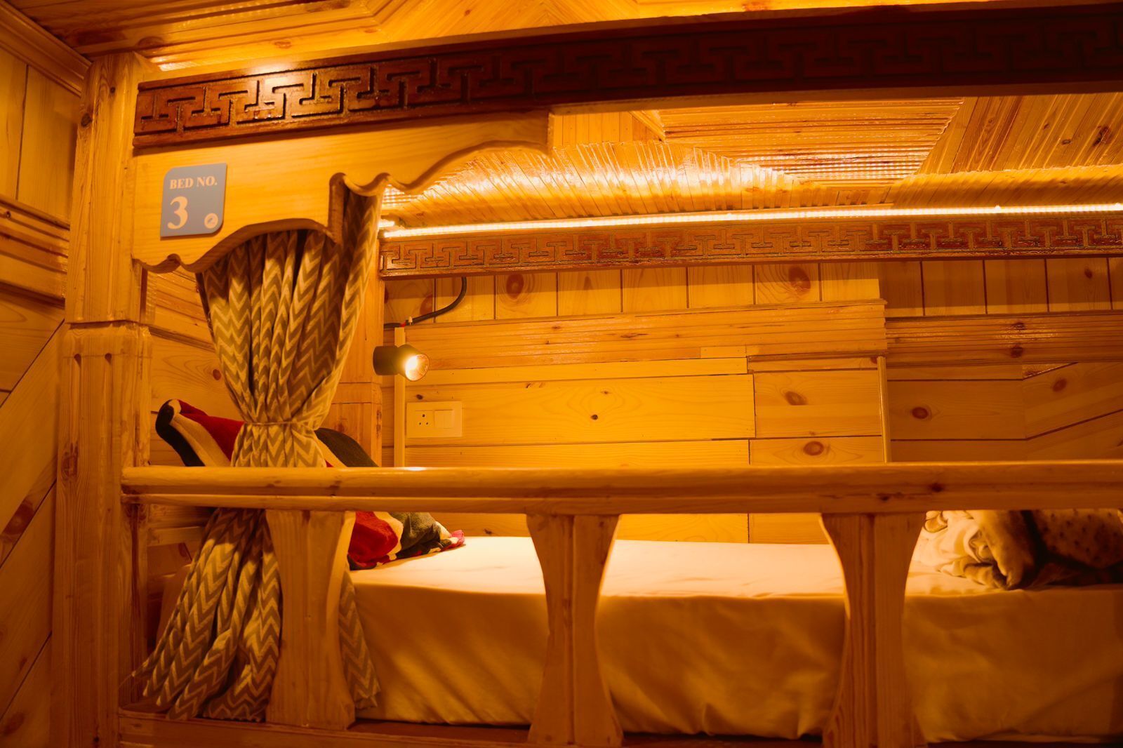 Quarto de cabana de madeira com beliches, placa de número de cama e uma luminária.