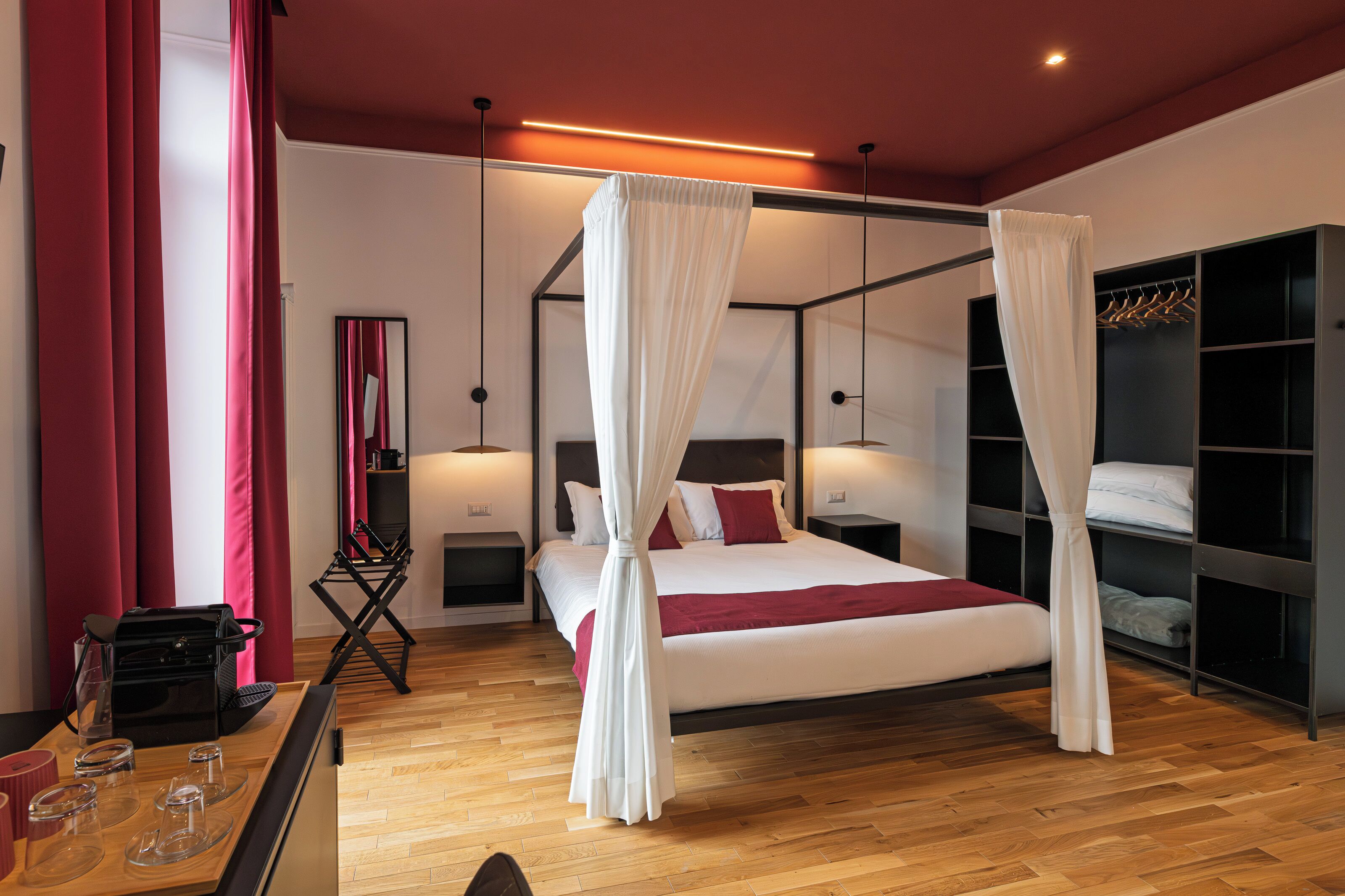Um quarto moderno com cama de dossel, mesa de cabeceira com copos, bandeja com copos e guarda-roupa.