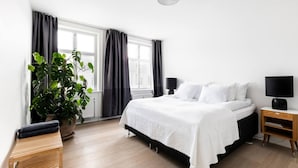 Quarto moderno com uma cama grande, mesa de cabeceira com abajur, planta em vaso e um banco.