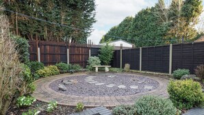 Um jardim circular com pedras no chão, cercado por muros de tijolo e diversas plantas.