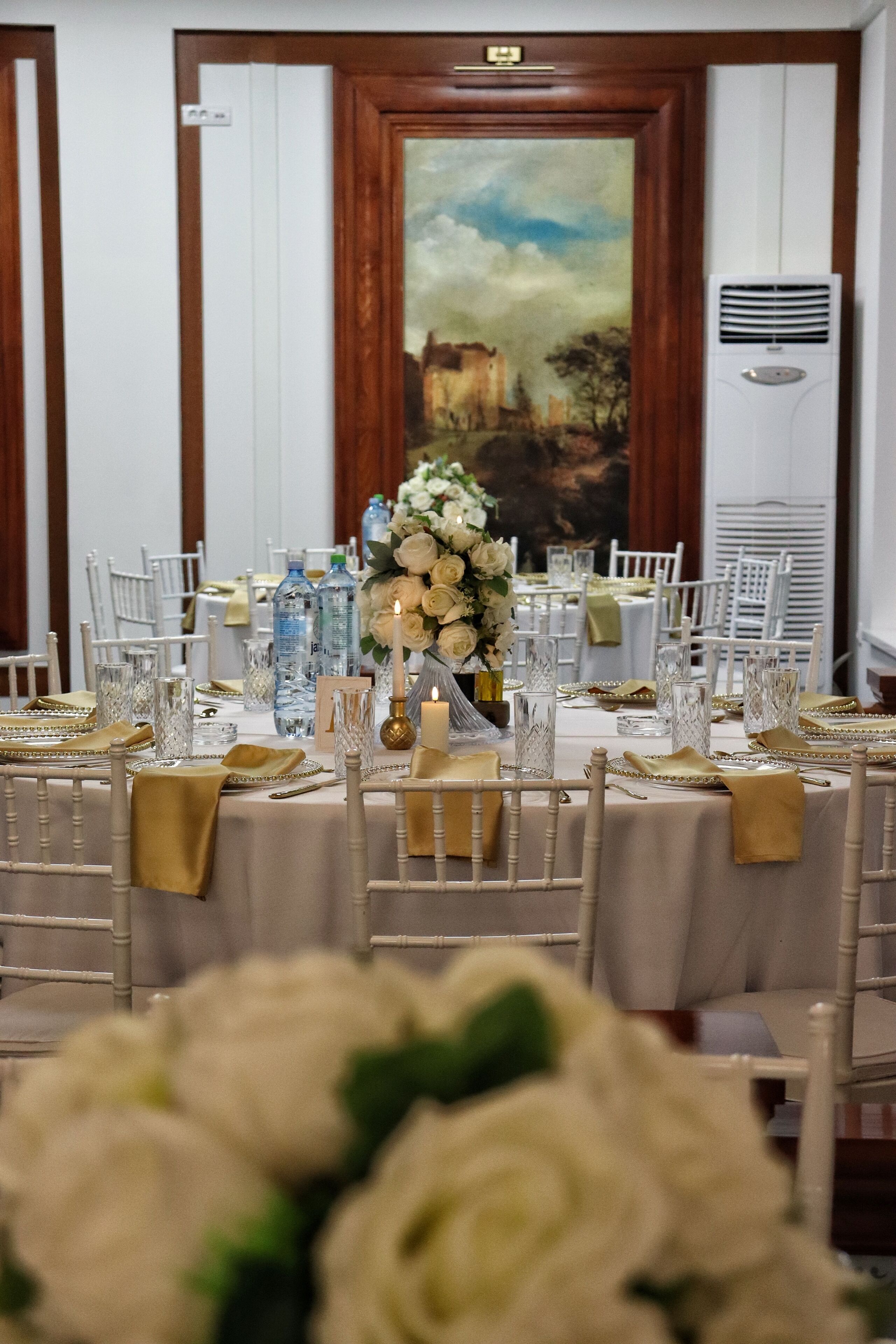 Uma sala de jantar formal com uma mesa comprida posta para uma refeição, cadeiras e um arranjo de flores.