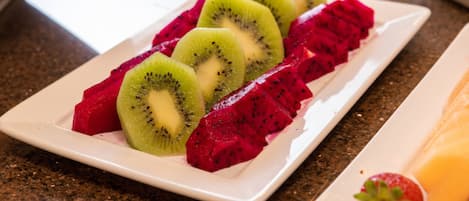 Prato branco retangular com kiwi fatiado e pitaya sobre bancada de granito.