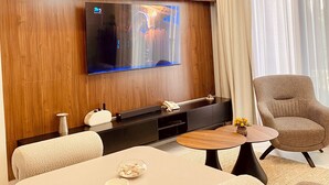 Uma sala de estar moderna com uma televisão de tela plana presa a uma parede de madeira, um sofá, uma mesa de jantar com um vaso de flores e uma pequena mesa lateral.