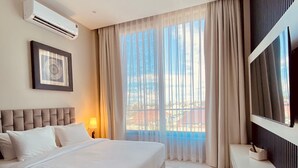 Quarto de hotel com cama, televisão, janela com cortinas e ar condicionado.