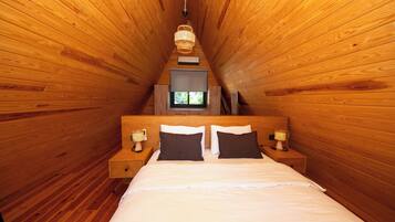 Um quarto de madeira com uma cama, duas luminárias de apoio, uma janela e um lustre.