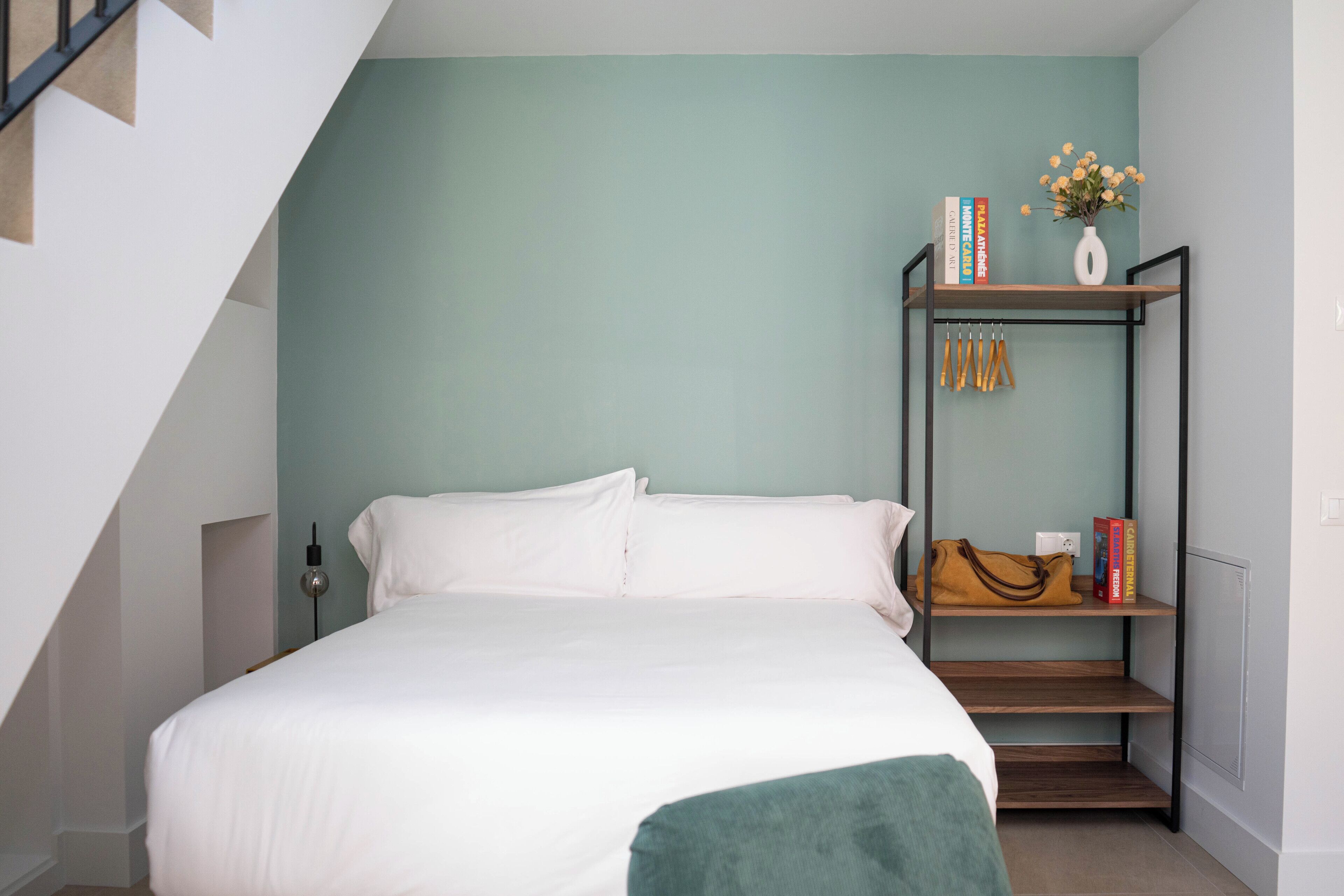 Quarto com cama, estante com livros e um vaso, e escada.