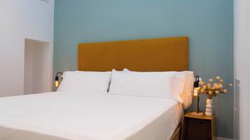 Cama bem arrumada com lençóis brancos, cabeceira de madeira e mesa de cabeceira com abajur e um vaso de flores.