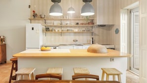 Uma cozinha com ilha central, banquetas de madeira, iluminação pendente e uma geladeira.