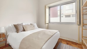Quarto com cama, mesa de cabeceira, luminária, janela e escada de madeira.