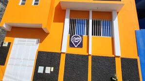 Um edifício de dois andares com fachada laranja vibrante, janelas brancas e uma parte inferior texturizada preta.