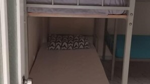 Quarto com beliche, porta à esquerda, travesseiro estampado na cama de baixo e parede lisa.