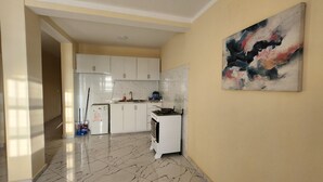 Cozinha com armários brancos, fogão e pia. Há um quadro na parede.