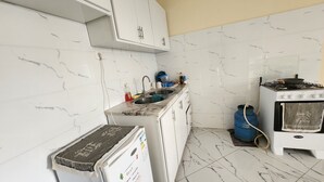Uma cozinha com ladrilhos de mármore branco, fogão a gás, pia e geladeira.
