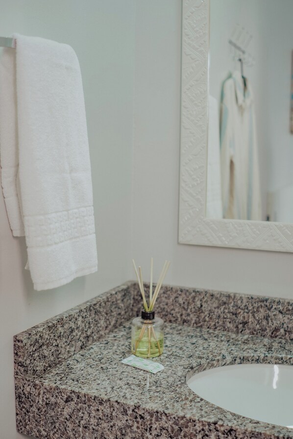 Um banheiro com bancada de granito, pia branca, toalha pendurada em um porta-toalhas e espelho com moldura decorativa.