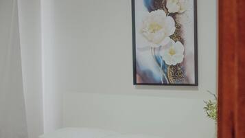 Quarto com duas camas, uma mesinha de cabeceira e uma pintura floral emoldurada na parede.