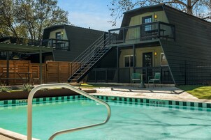 Uma área de piscina com deck claro, um conjunto de degraus que levam a uma varanda e uma área cercada com mobiliário de jardim.