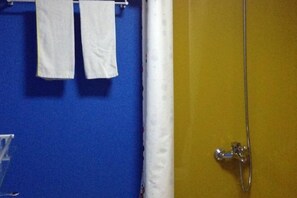 Casa de banho com parede azul, toalha branca pendurada num suporte e chuveiro com detalhes cromados.