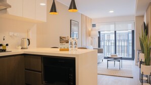 Uma cozinha moderna com ilha central, luminárias pendentes e vista para uma sala de estar com sofá e mesa de jantar.
