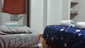 Quarto com duas camas, uma com colcha estampada de estrelas coloridas e outra com colcha azul e estrelas brancas. Há uma toalha branca sobre a cama com a colcha azul.
