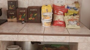 Uma bancada de cozinha com diversos alimentos e recipientes, incluindo caixas com as etiquetas 'TE', 'CAFÉ', 'AÇÚCAR' e 'FARINHA'.