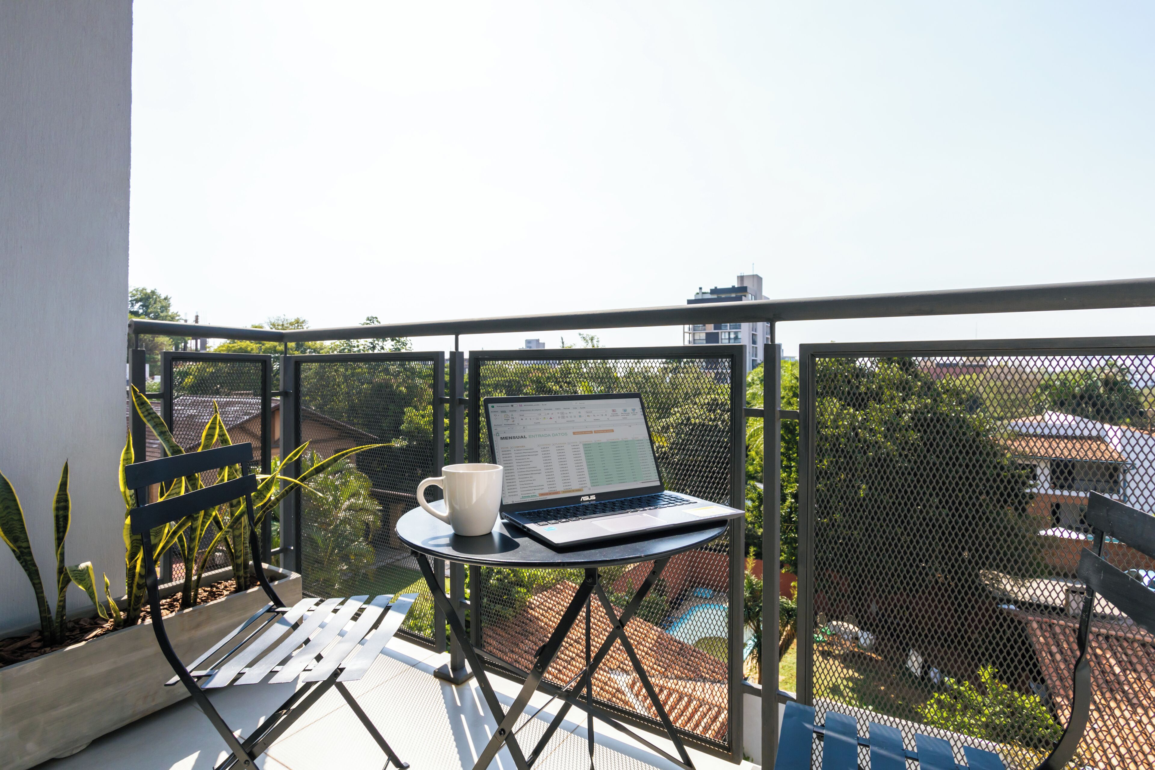 Uma varanda com um laptop, uma chávena e uma cadeira.