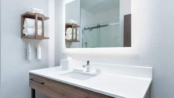 Um banheiro moderno com toucador branco, um espelho grande, box de chuveiro em vidro e porta-toalhas de madeira.