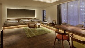 Quarto de hotel moderno com uma cama grande, área de refeições, espaço de estar e uma janela ampla com cortinas.