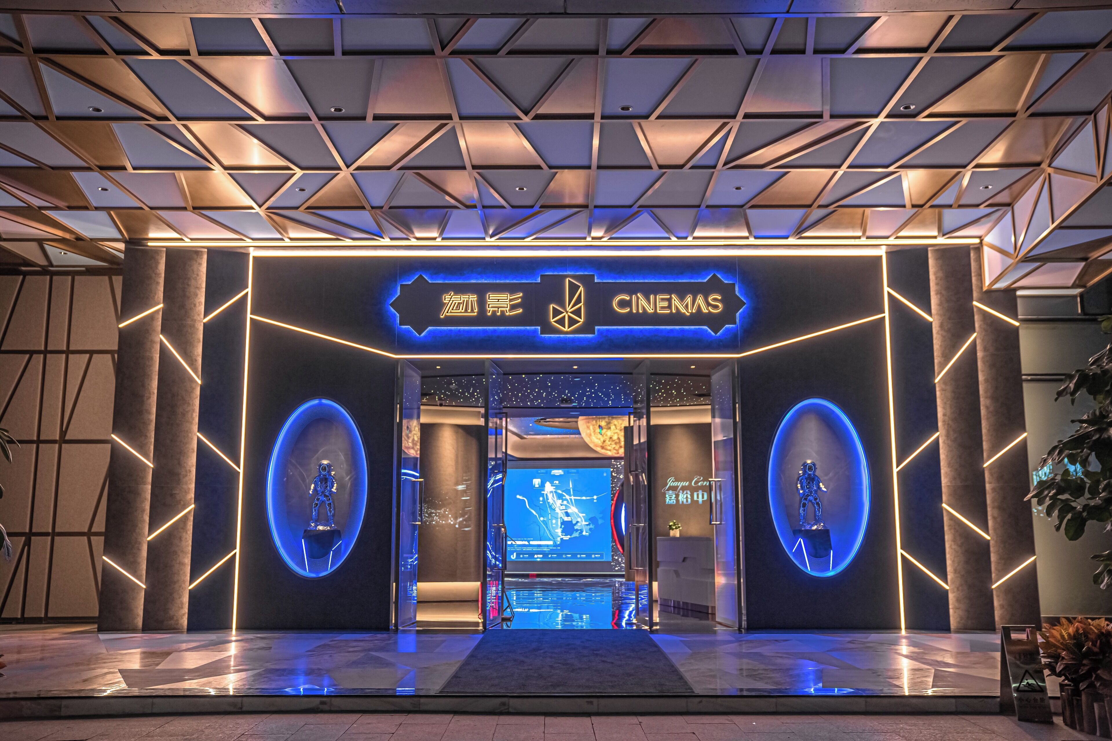Entrada de cinema com design moderno, com letreiros iluminados e padrões geométricos no teto.