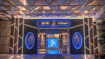 Entrada de cinema com design moderno, com letreiros iluminados e padrões geométricos no teto.
