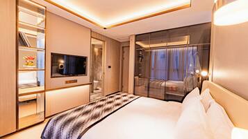 Quarto de hotel moderno com uma cama grande, televisão, guarda-roupa e casa de banho visível através de um painel de vidro.