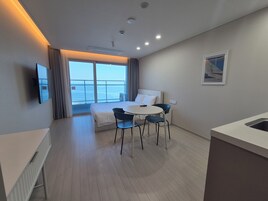 Quarto de hotel com cama, mesa de jantar com cadeiras, televisão e vista para o mar.