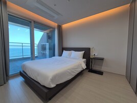 Quarto de hotel moderno com uma cama grande, uma escrivaninha e vista para o mar.