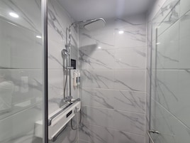 Um banheiro moderno com chuveiro em box de vidro, azulejos de mármore e chuveiro manual.