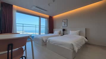 Quarto de hotel com duas camas, uma mesa e vista para o oceano.