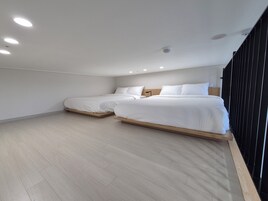 Quarto moderno com duas camas, piso de madeira e iluminação embutida no teto.