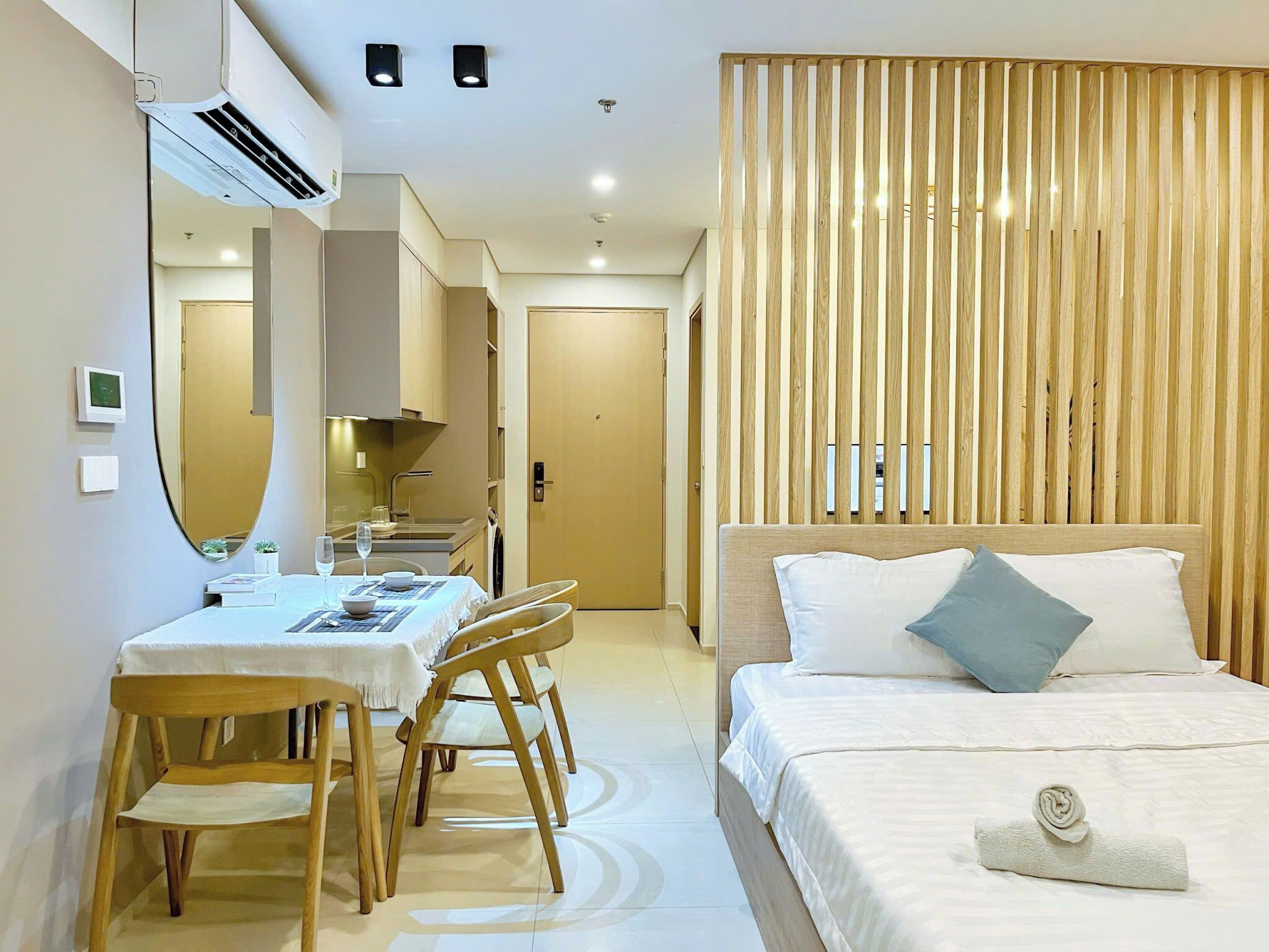 Quarto de hotel com cama, mesa de jantar com cadeiras, cozinha e divisória de madeira.
