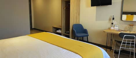 Quarto de hotel com cama, escrivaninha, cadeira, televisão e guarda-roupa.